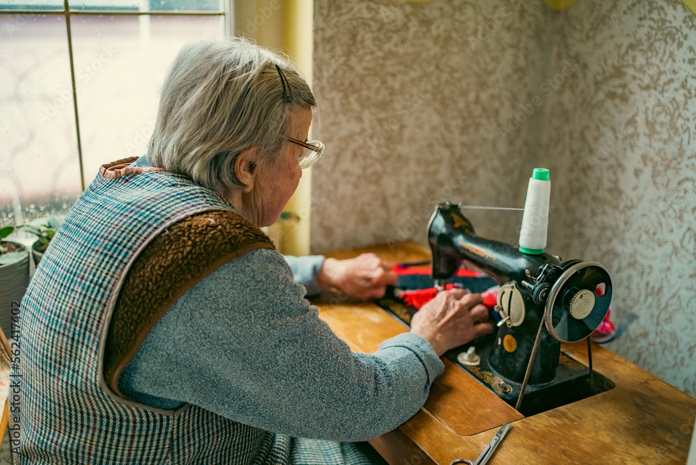 Foto de Senior woman in spectacles use sewing machine. wrinkled hands ...