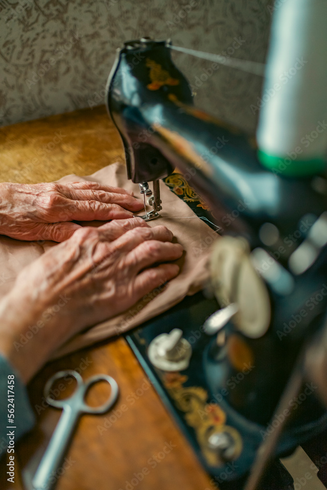 Senior woman in spectacles use sewing machine. wrinkled hands of the ...