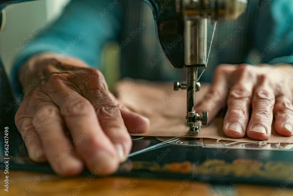 Senior woman in spectacles use sewing machine. wrinkled hands of the ...