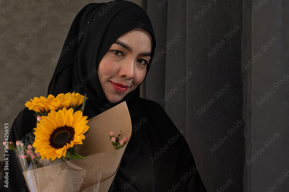 Foto de Muslim woman wearing black hijab holding bouquet of sunflowers ...
