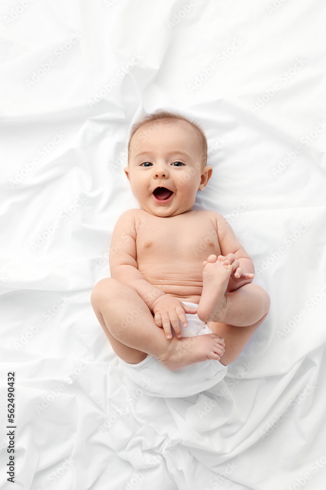 Happy newborn baby in diaper lying on white sheet grabbing feet Stock Photo | Adobe Stock