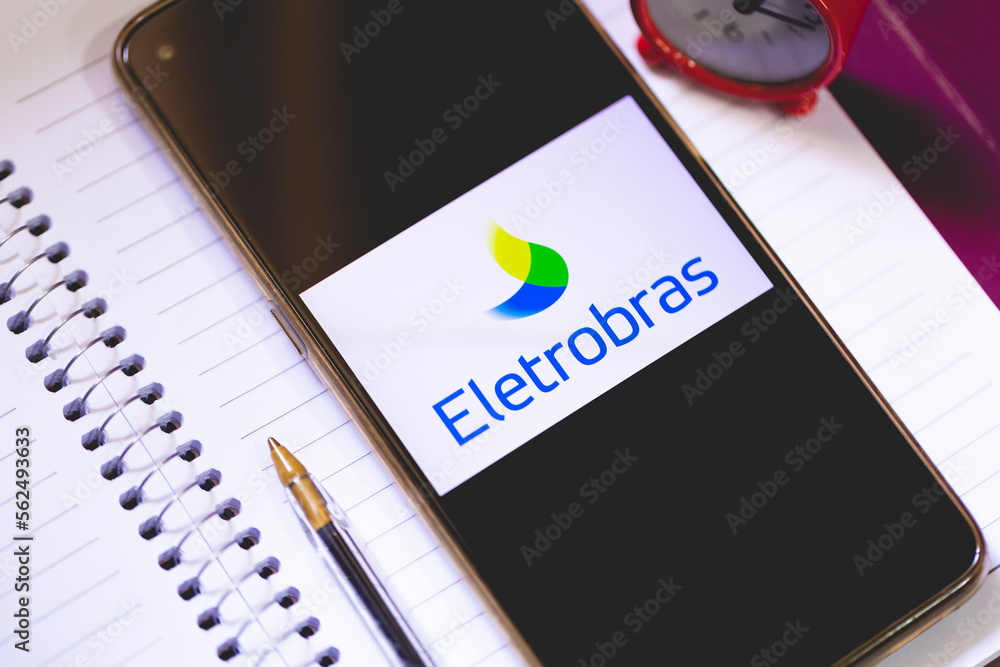 A logo da Eletrobras na tela de um telefone celular. Um caderno e uma ...