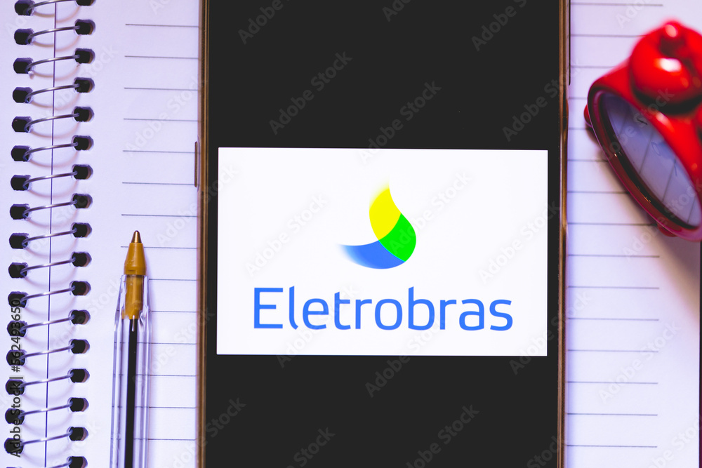 A logo da Eletrobras na tela de um telefone celular. Um caderno e uma ...