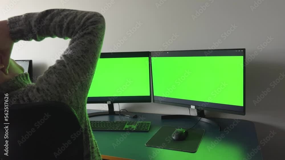 an office worker sits in front of two monitors with chromakey green ...