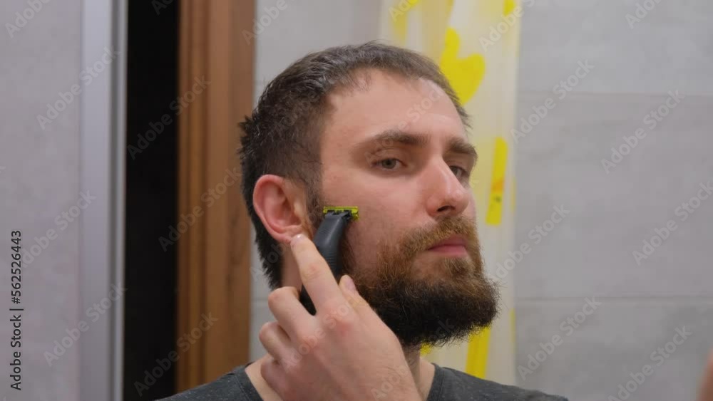 The man shaves his big beard. The guy shaves off his big beard. Young ... The man shaves his big beard. The guy shaves off his big beard. Young ...
