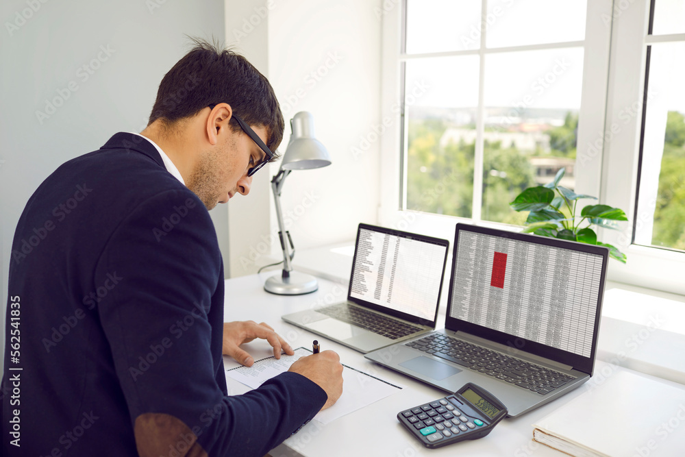 Financial accountant working in modern office. Busy man in suit and glasses sitting at desk by ...