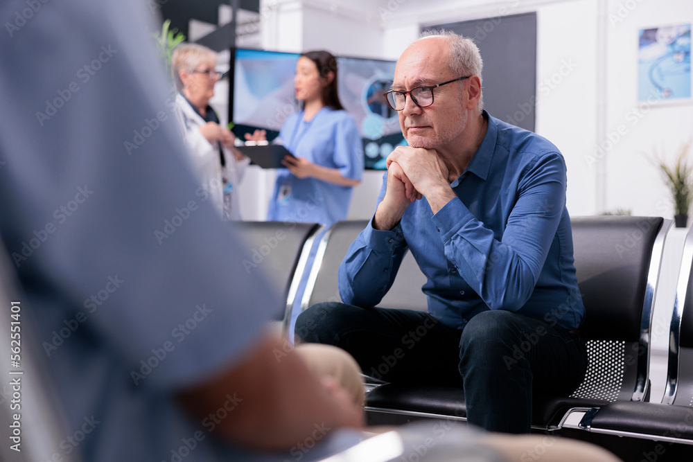 Stressed tired senior patient sitting on chair in hospital lobby while ...