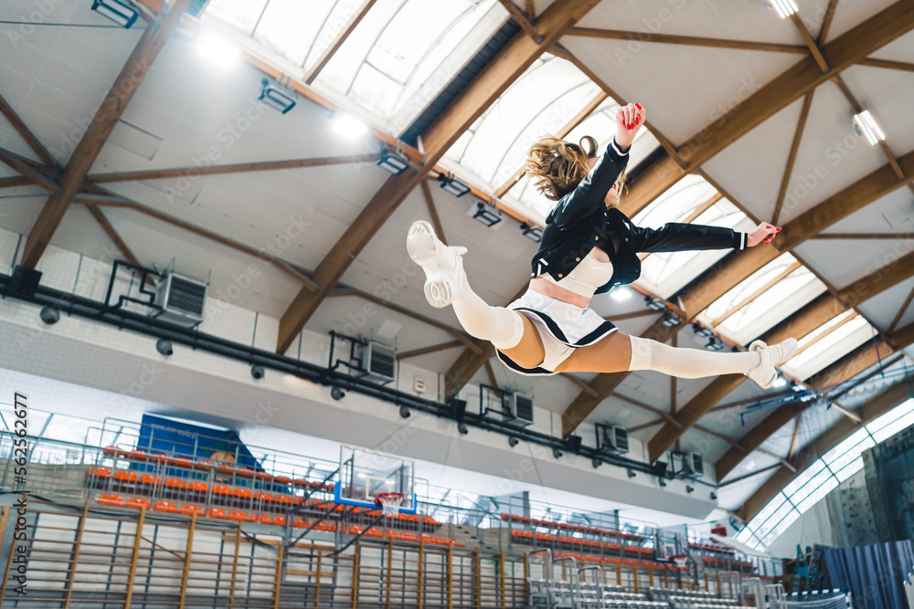 Side view of a cheerleader in the sports hall doing a split in the air ...