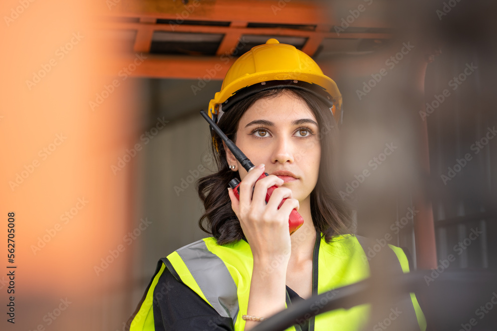 Female foreman using radio while driving forklift vehicle at shipping ...