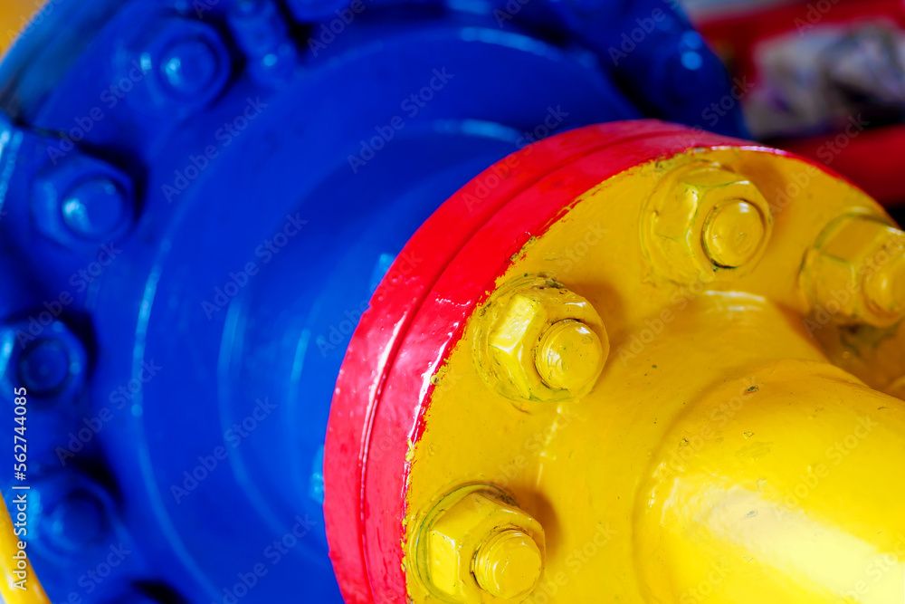 Two blue and yellow gas pipes are connected by large bolts and nuts ...