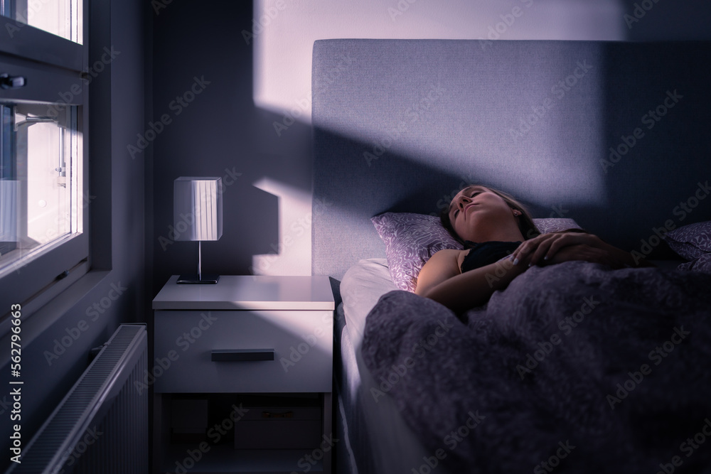 Sleeping woman in bed at night in dark bedroom. Person under blanket ...