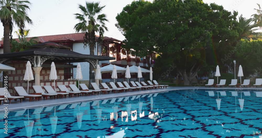 Luxury resort pool scene with empty deck chairs and folded parasols ...