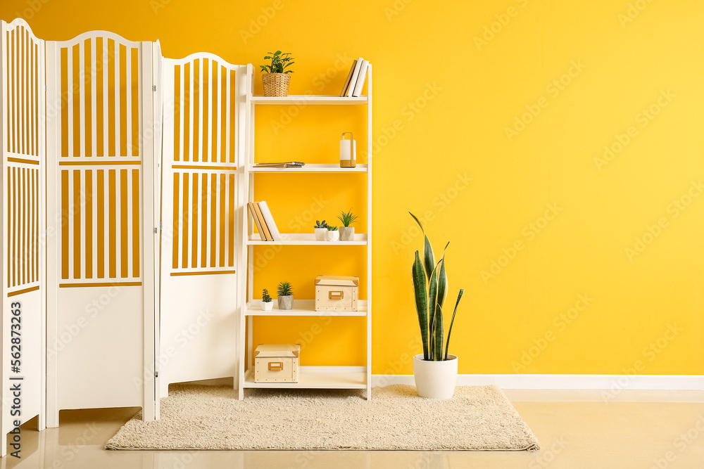 Interior of room with folding screen, shelving unit and houseplant near ...