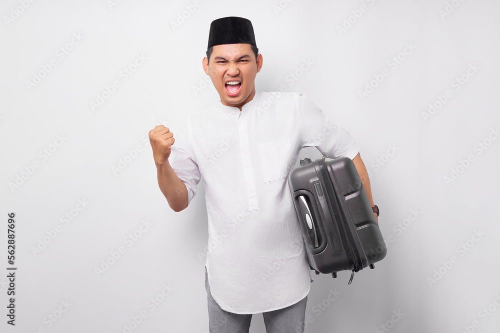 Excited young Asian Muslim man standing while holding a suitcase in ...