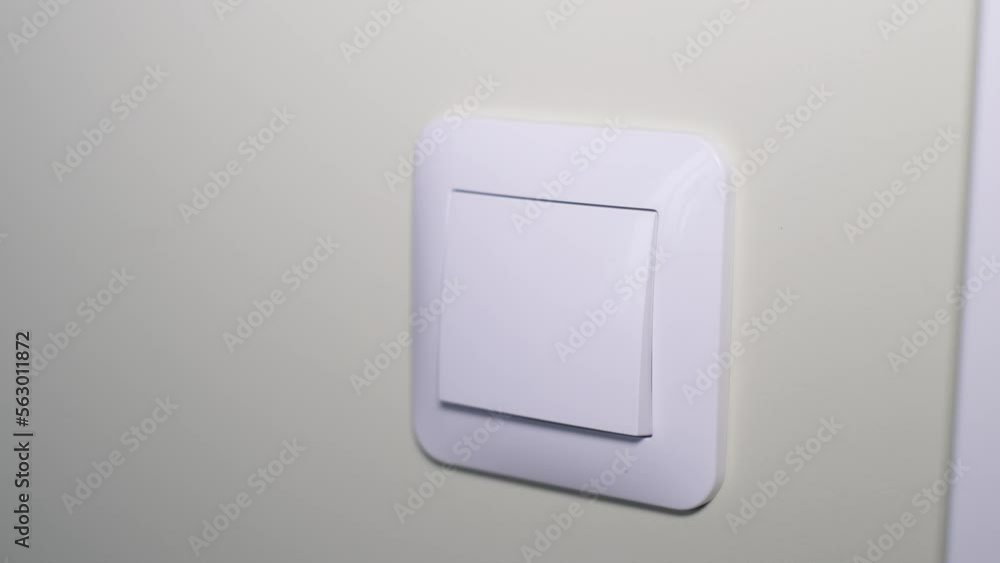 Close-up of a light switch on the wall being turned on by a woman's ...
