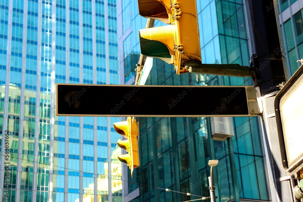 Black empty street sign underneath a yellow traffic light in front of ...