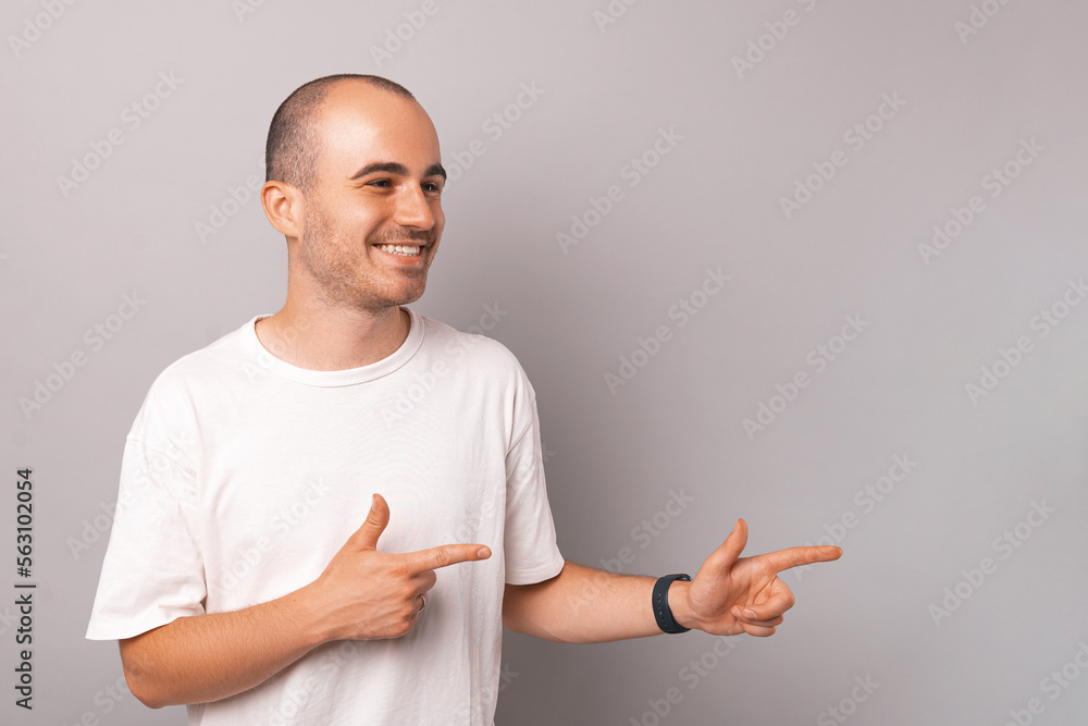 Handsome young man is pointing aside with two hands over grey ...