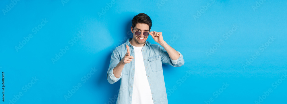 Handsome cheeky guy in sunglasses, smiling and pointing finger gun at ...