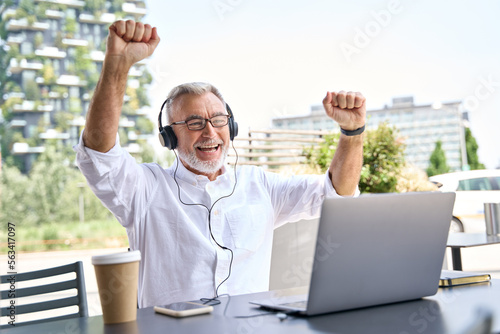 Happy older senior business man using laptop wearing headphones raising ...
