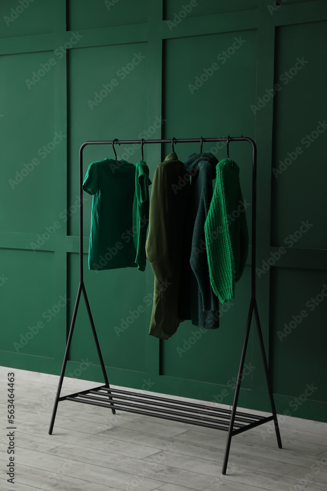 Rack with stylish female clothes near green wall Stock Photo | Adobe Stock