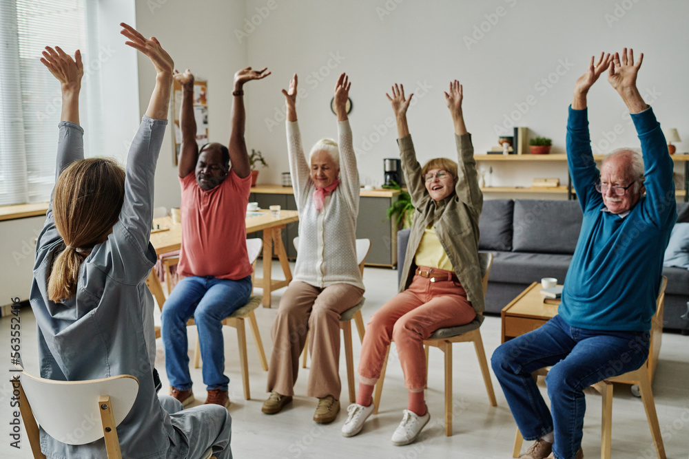 Group of senior people sitting on chairs and exercising during sport ...