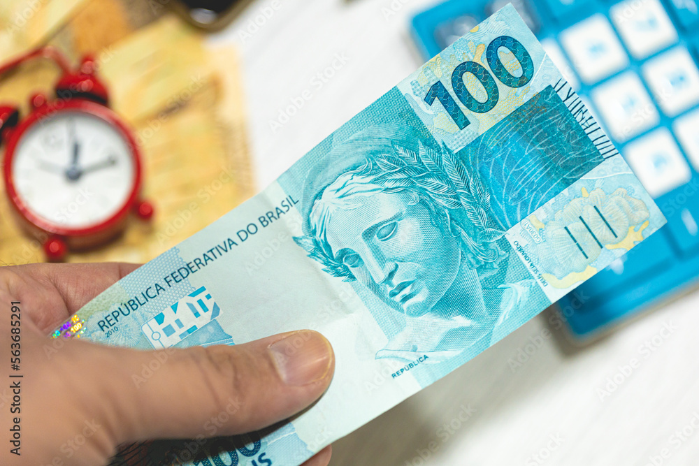 Um homem segurando uma nota do Real Brasileiro no valor de 100 Reais ...