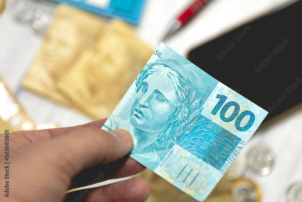 Um homem segurando uma nota do Real Brasileiro no valor de 100 Reais ...