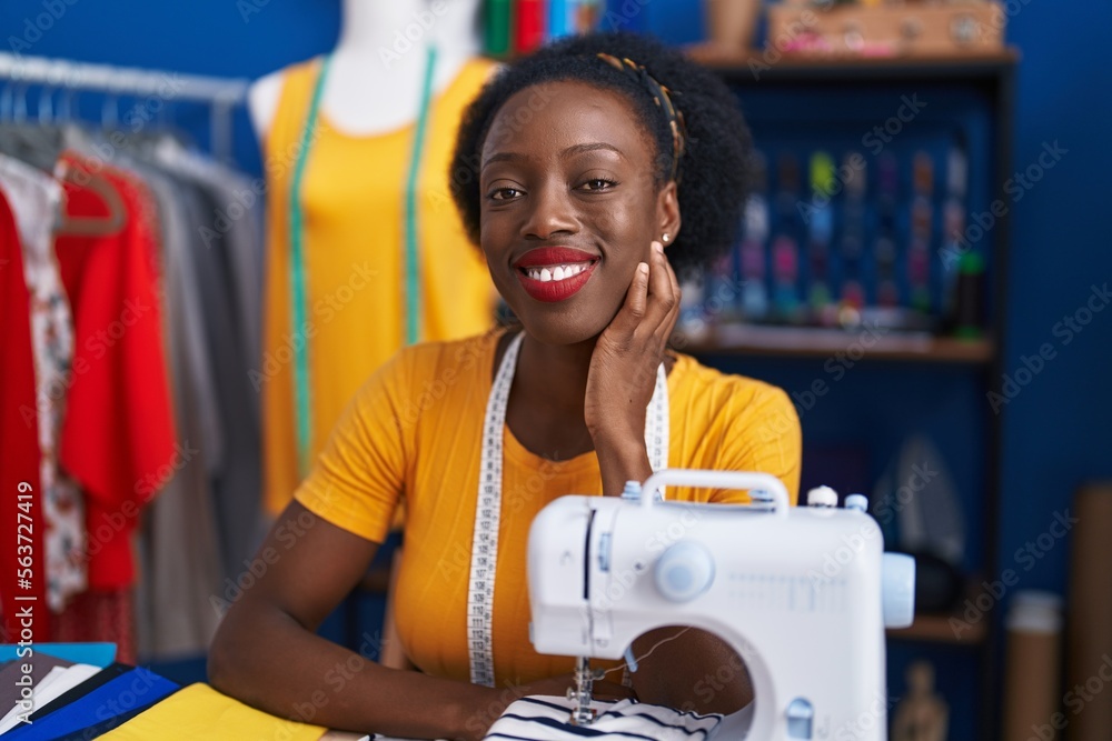 African american woman tailor smiling confident using sewing machine at ...