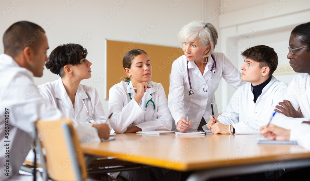 Group of medical students in white coats studying in classroom. Senior ...