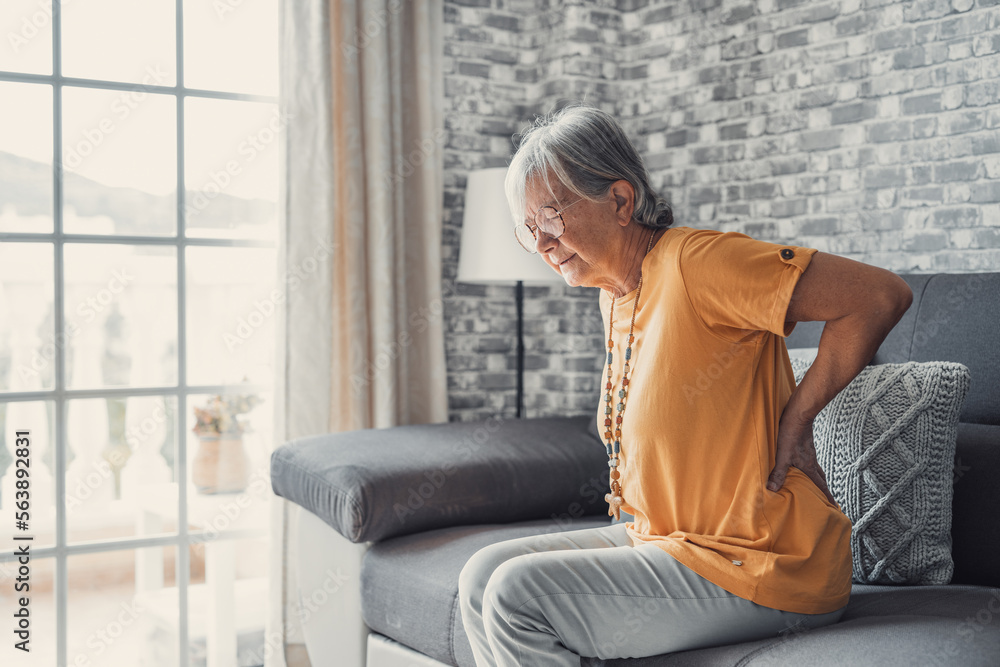 Unhappy mature woman touching back, feeling pain, sitting on couch in ...