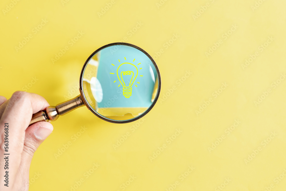 Light bulb hiding of yellow punched paper, Hand holding magnifier focus ...