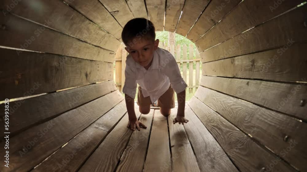 Little boy crawling on all fours through wooden tube on the playground ...