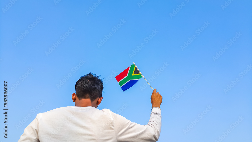 Boy holding South Africa flag against clear blue sky. Man hand waving ...