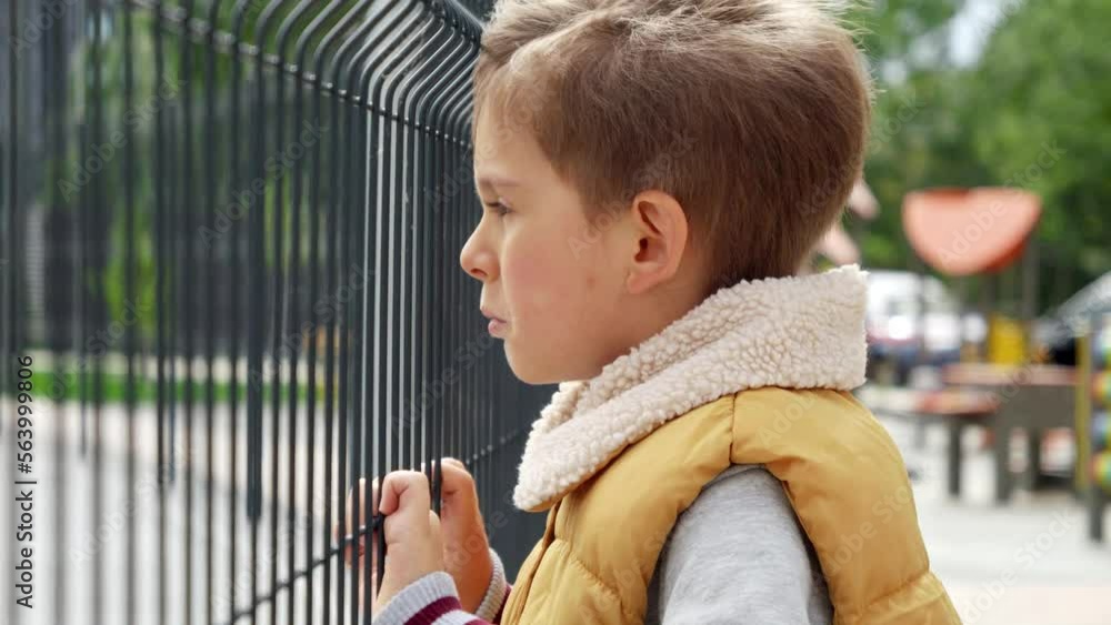 Little boy feeling sad and alone looking through metal fence on ...