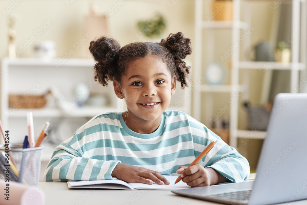 Cute black girl doing homework at desk and smiling at camera in home ...