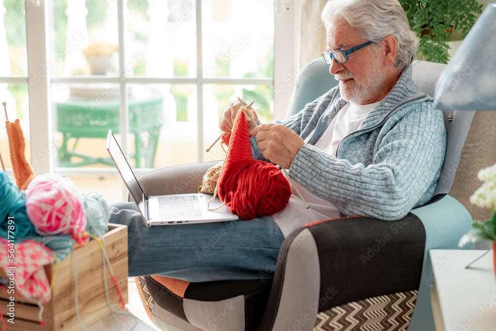 Portrait of senior man sitting on the armchair at home knitting ...