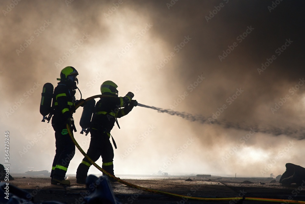 Silhouettes of firemen in smoke, using water to extinguish a massive ...