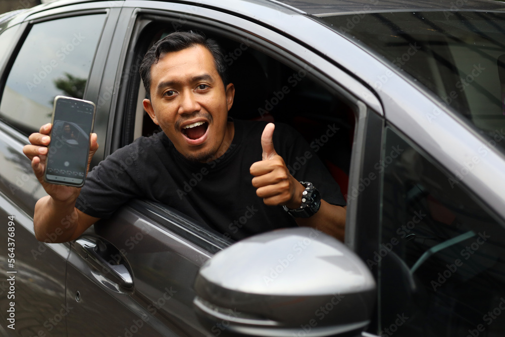 Happy asian driver pointing his cell phone screen and showing thumbs up ...