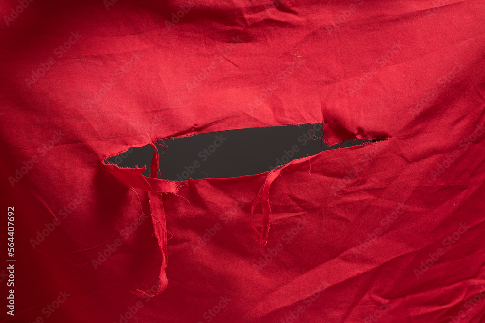 red fabric with big hole and shredded threads, ripped open hole at ...