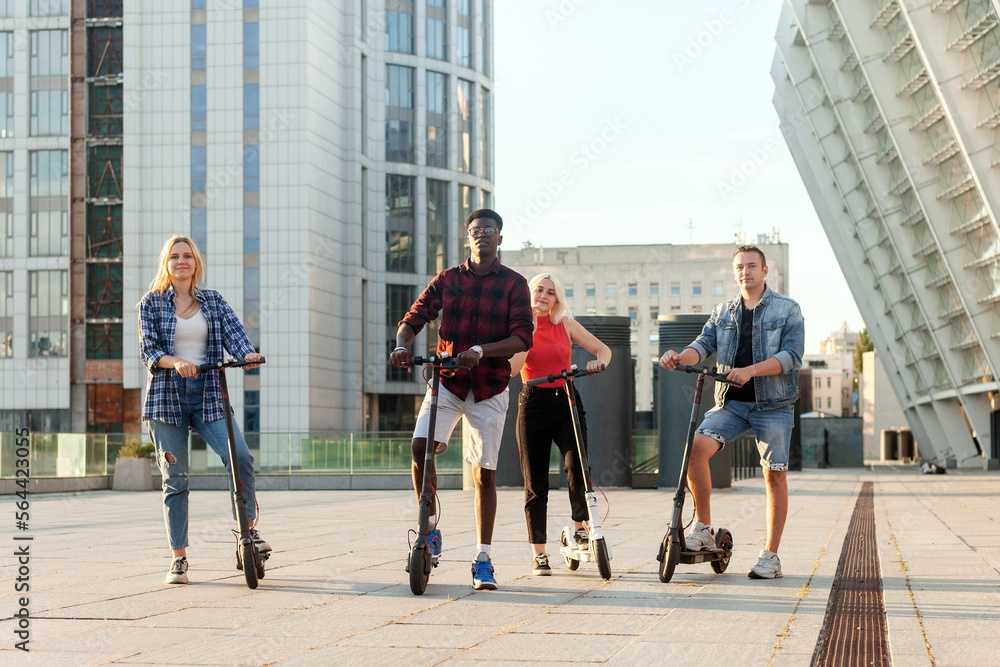 interracial group of friends ride electric scooters in the city ...