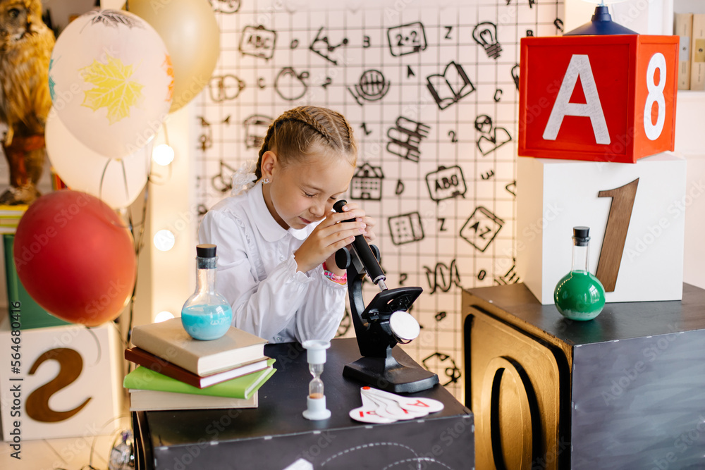 Schoolgirl in the lesson with a microscope. Smart child is learning ...