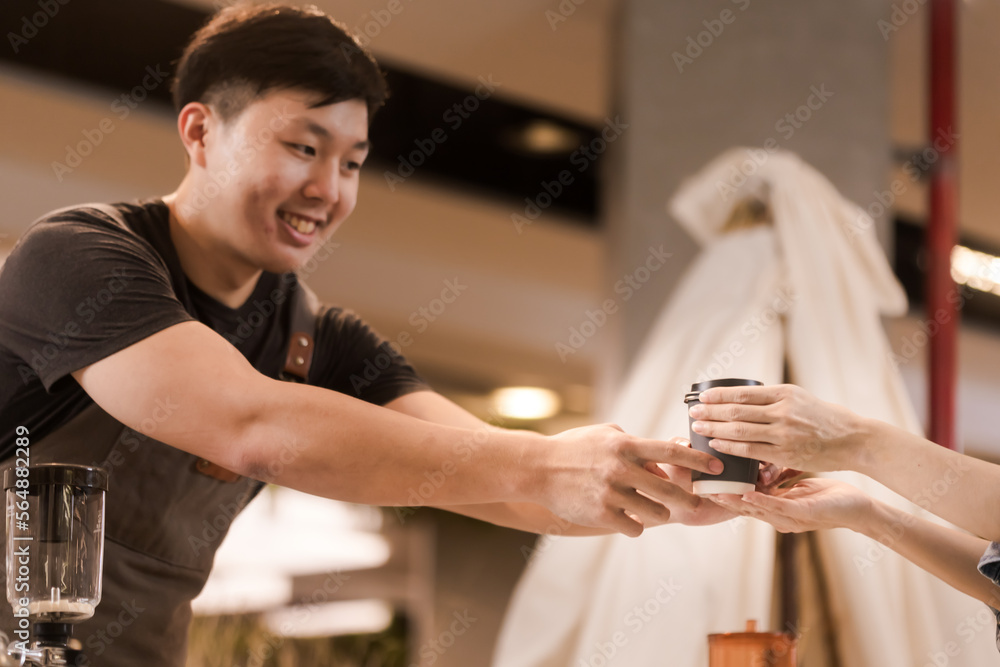 Asian man, coffee maker, handing over a cup of coffee Served to female ...