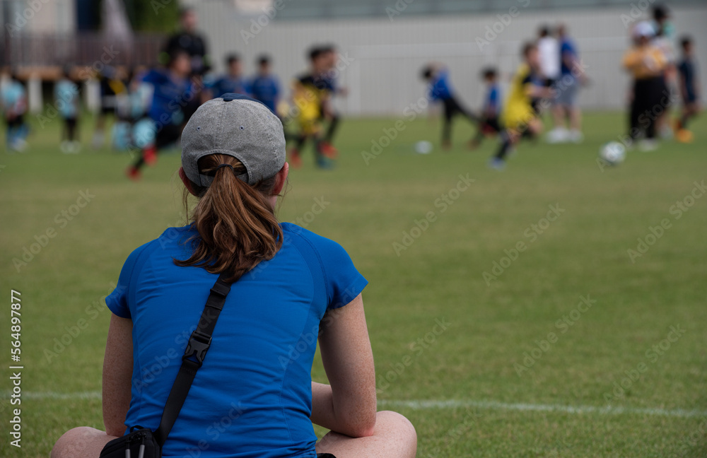 Mom sitting and watching her son playing football in a school football ...