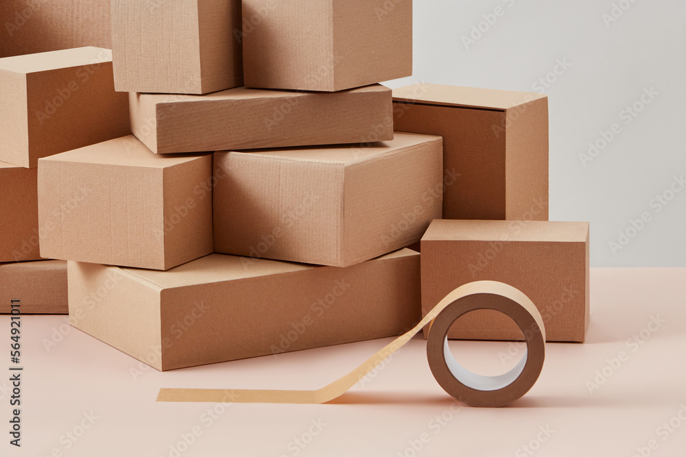 Packing tape in front of stacked cardboard boxes. Stock Photo | Adobe Stock