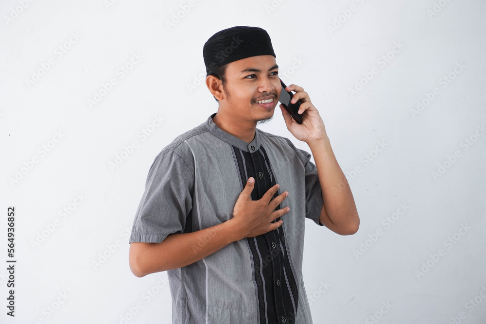 smiling young asian muslim man holding chest and holding phone calling ...