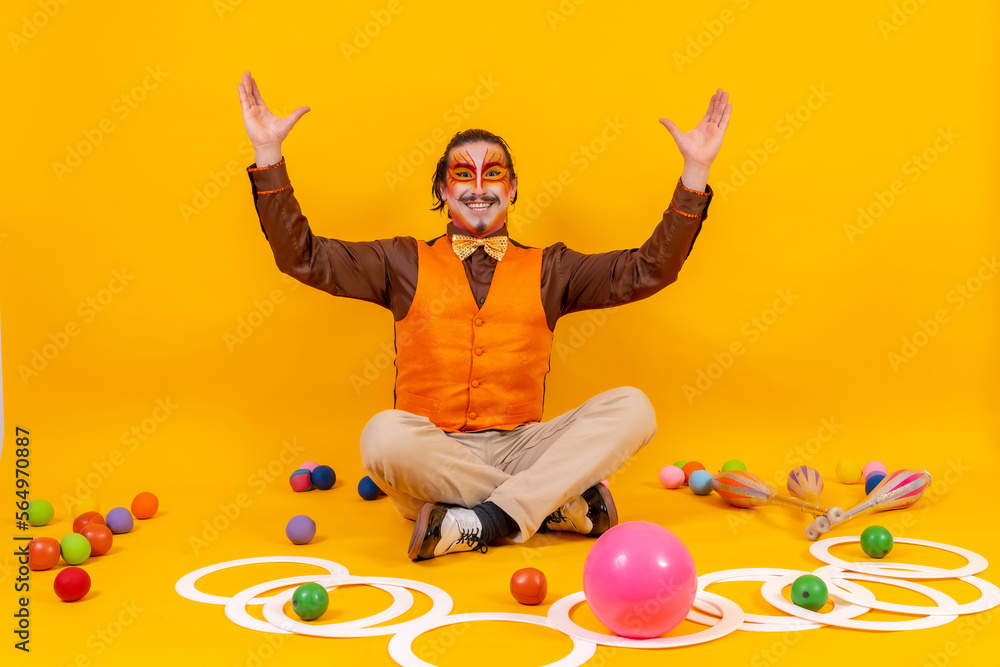 Juggler in a vest and with his face painted sitting with the juggling ...