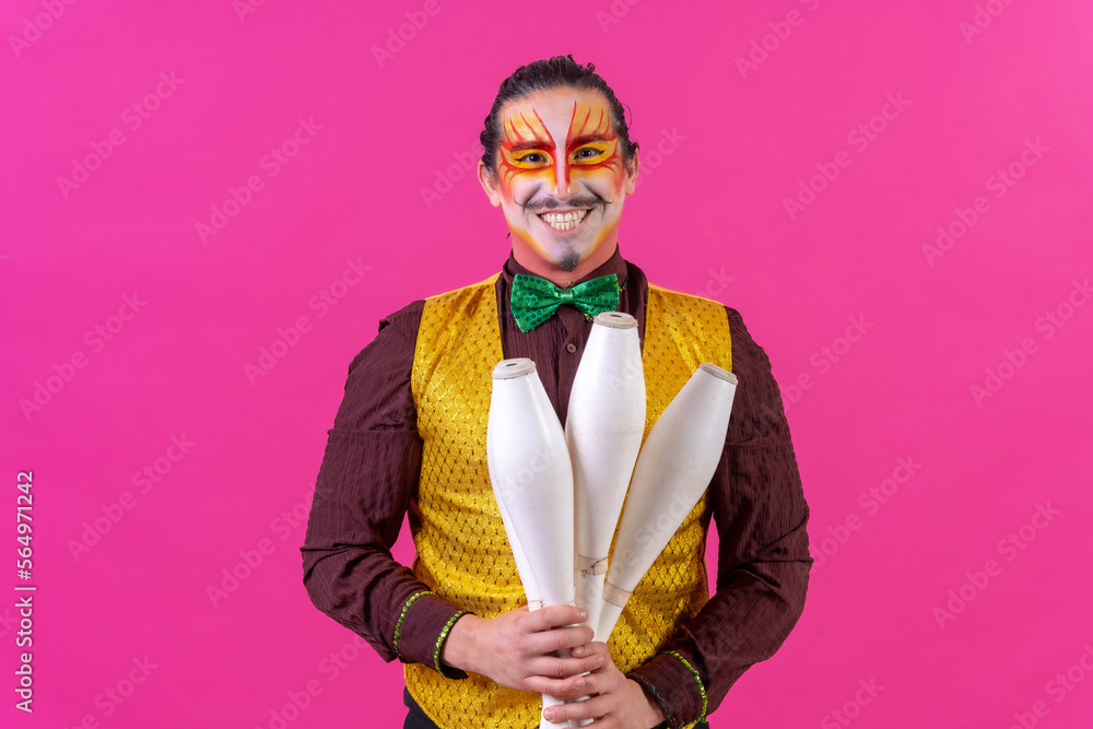 Juggler in a vest and with painted face juggling maces on a pink ...