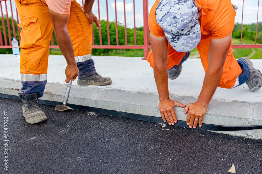 Workers apply black bitumen membrane strips for waterproofing roads and ...