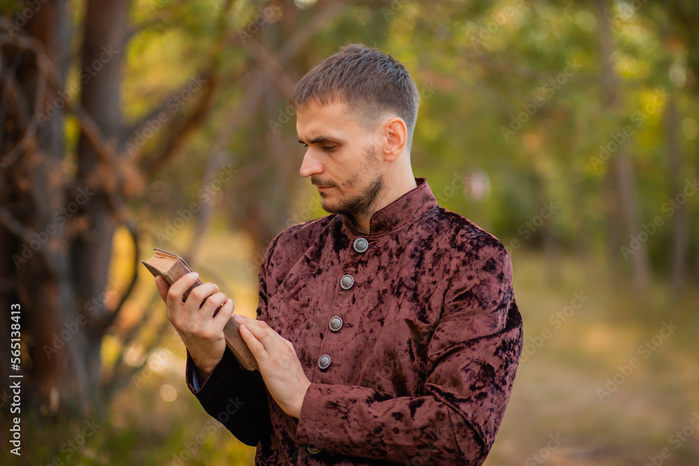 A young man in medieval brown clothes stands with an old book in his ...