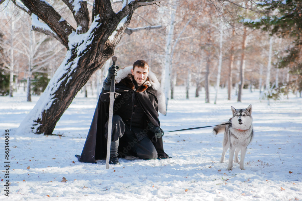 Handsome male warrior with a sword in winter near a snow-covered tree ...
